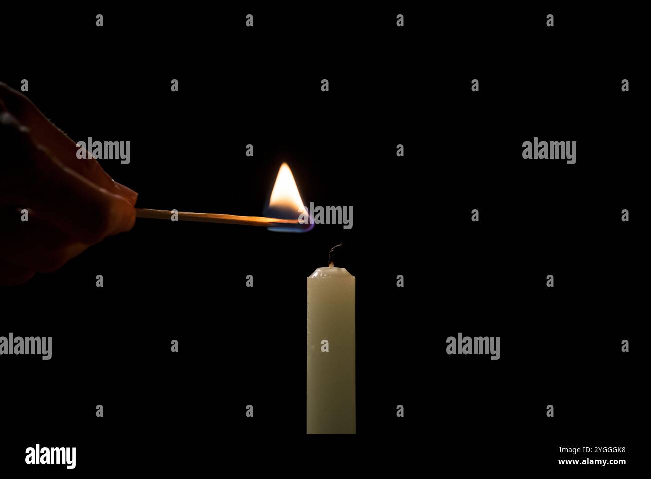 Male hand lighting a white thin taper candle using a safety match on a ...