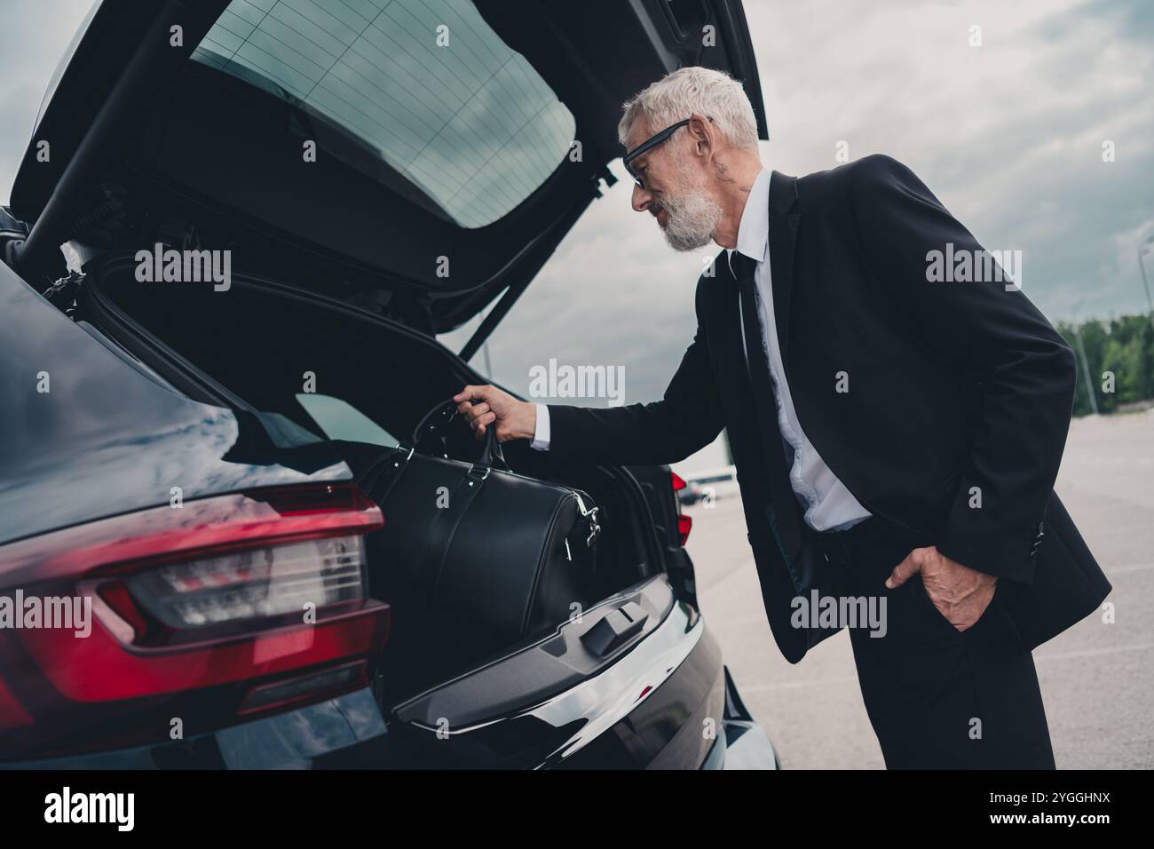 Senior businessman in formal wear loading suitcase into car on city ...