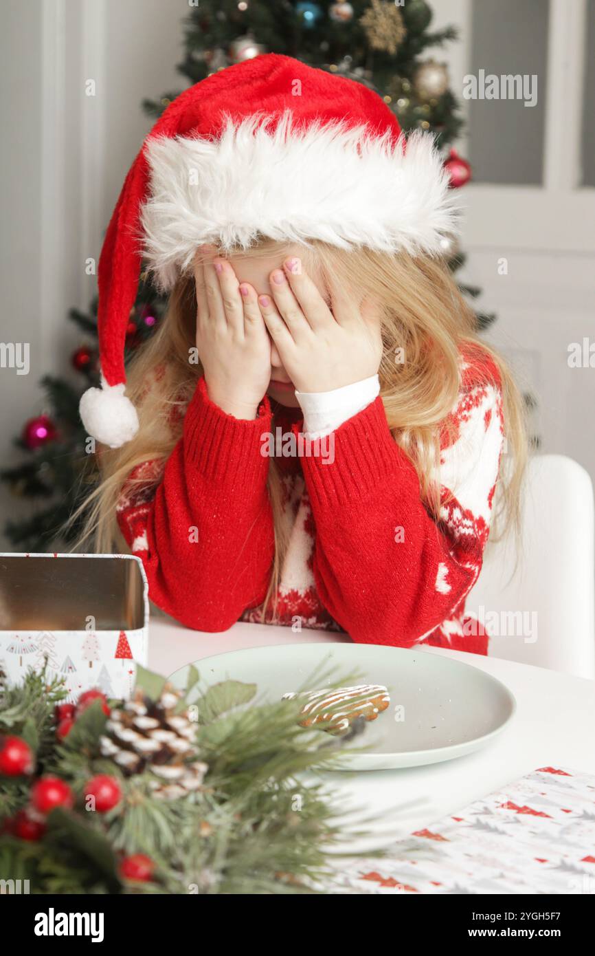 Sad, frustrated little girl in Christmas outfit and Santa hat sitting ...