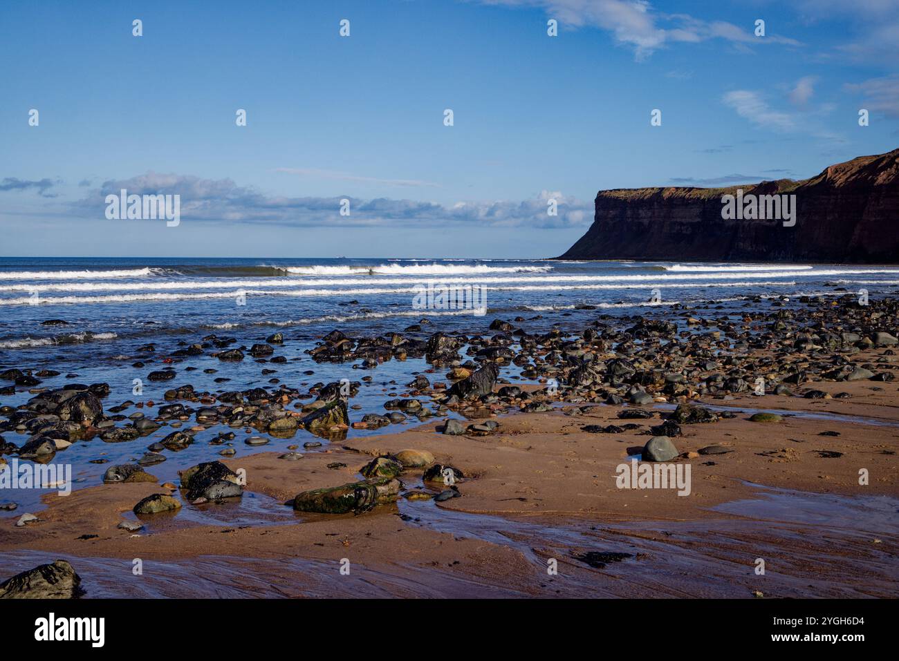 Rocks dotted around the sandy beach below the looming Hunt Cliff ...