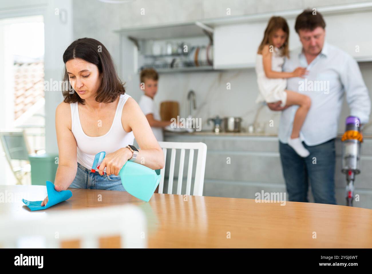 Wife cleans table with rag, husband and children clean kitchen in ...