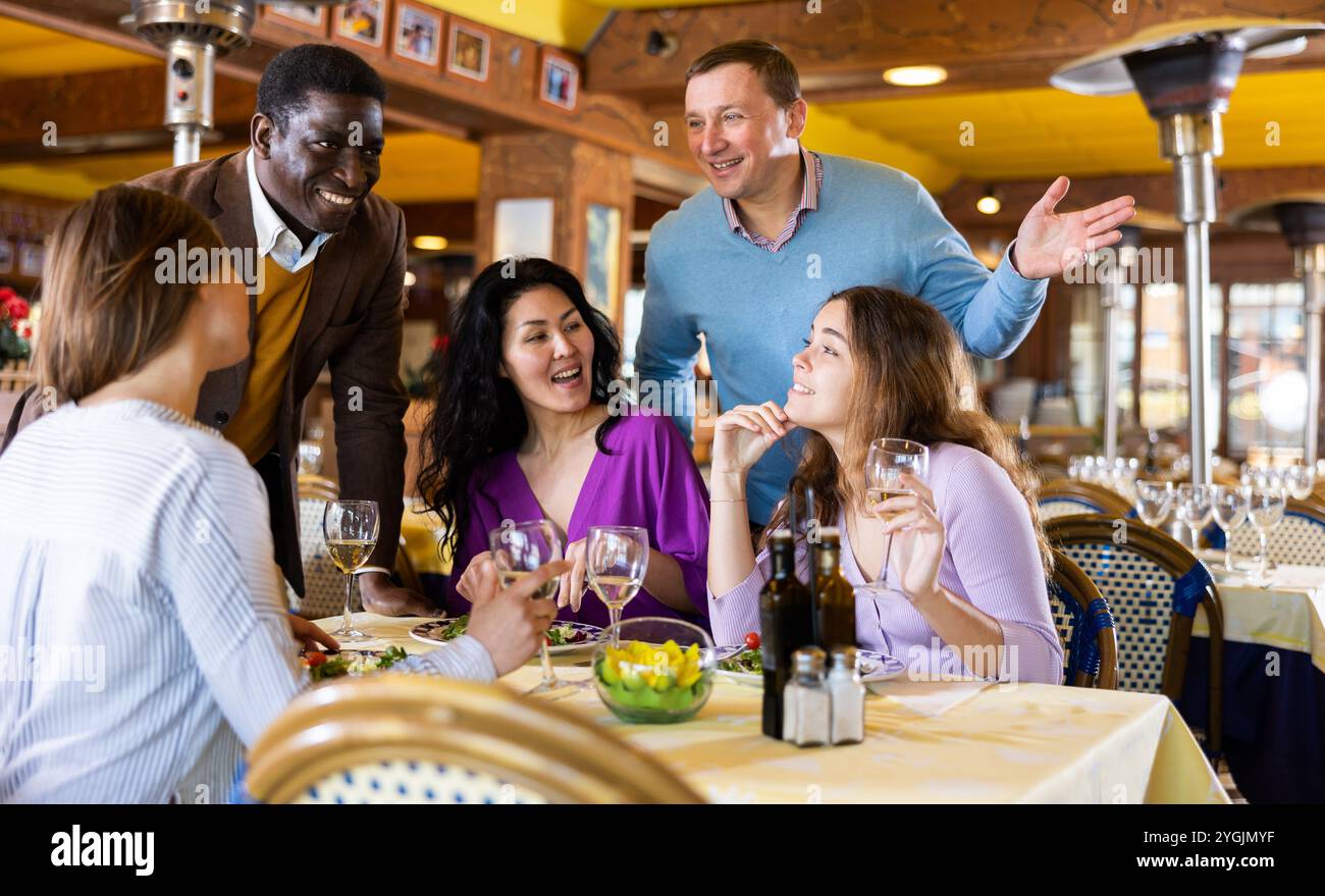 Smiling men invite women to dine for their table in restaurant Stock ...