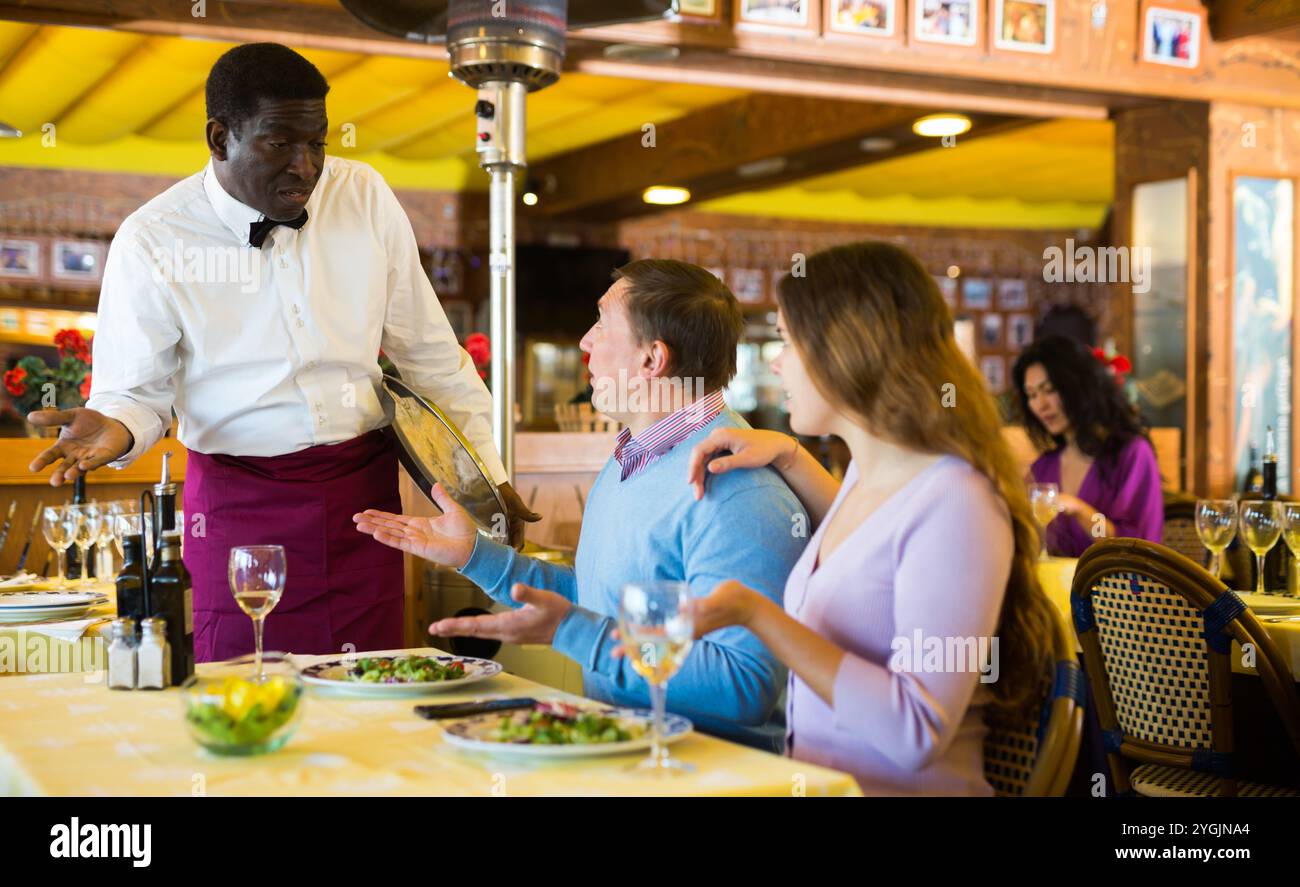 Displeased guests conflicting with waiter Stock Photo - Alamy