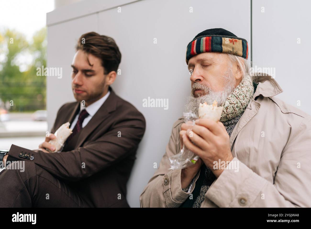 Kind young businessman in suit and elderly homeless man eating together ...