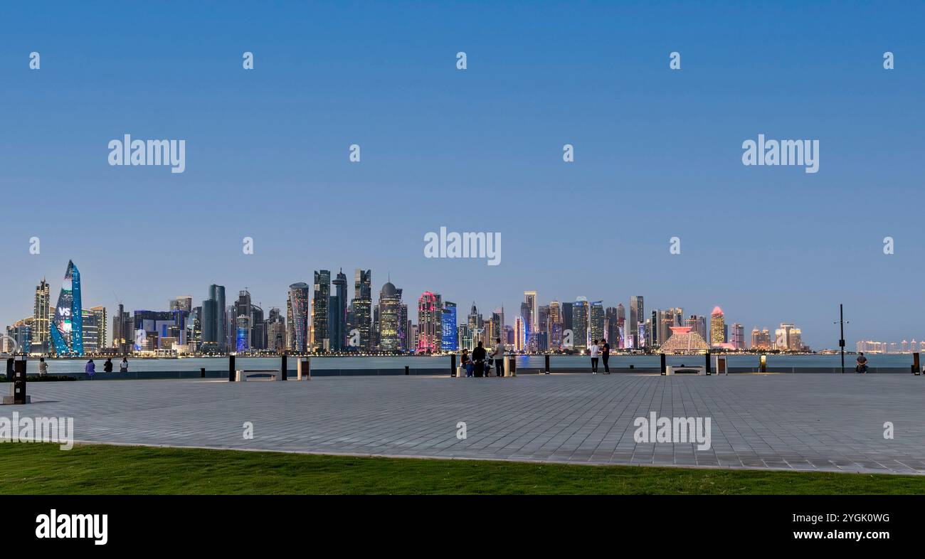 People on the shore, in the background the skyline of Doha at dusk ...