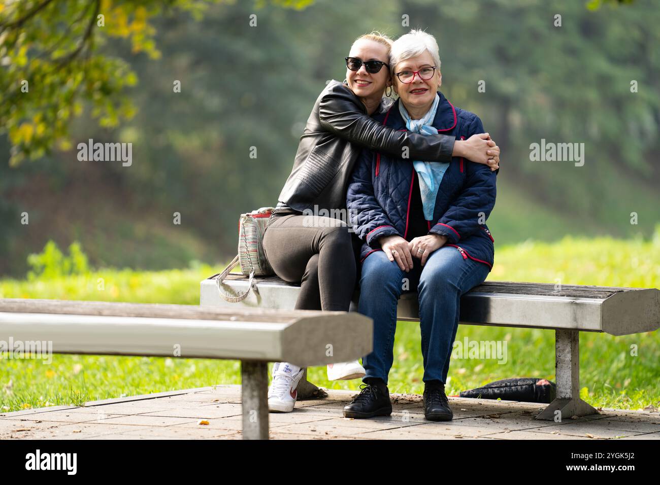 A gray-haired senior and her daughter relax in a park, enjoying the ...