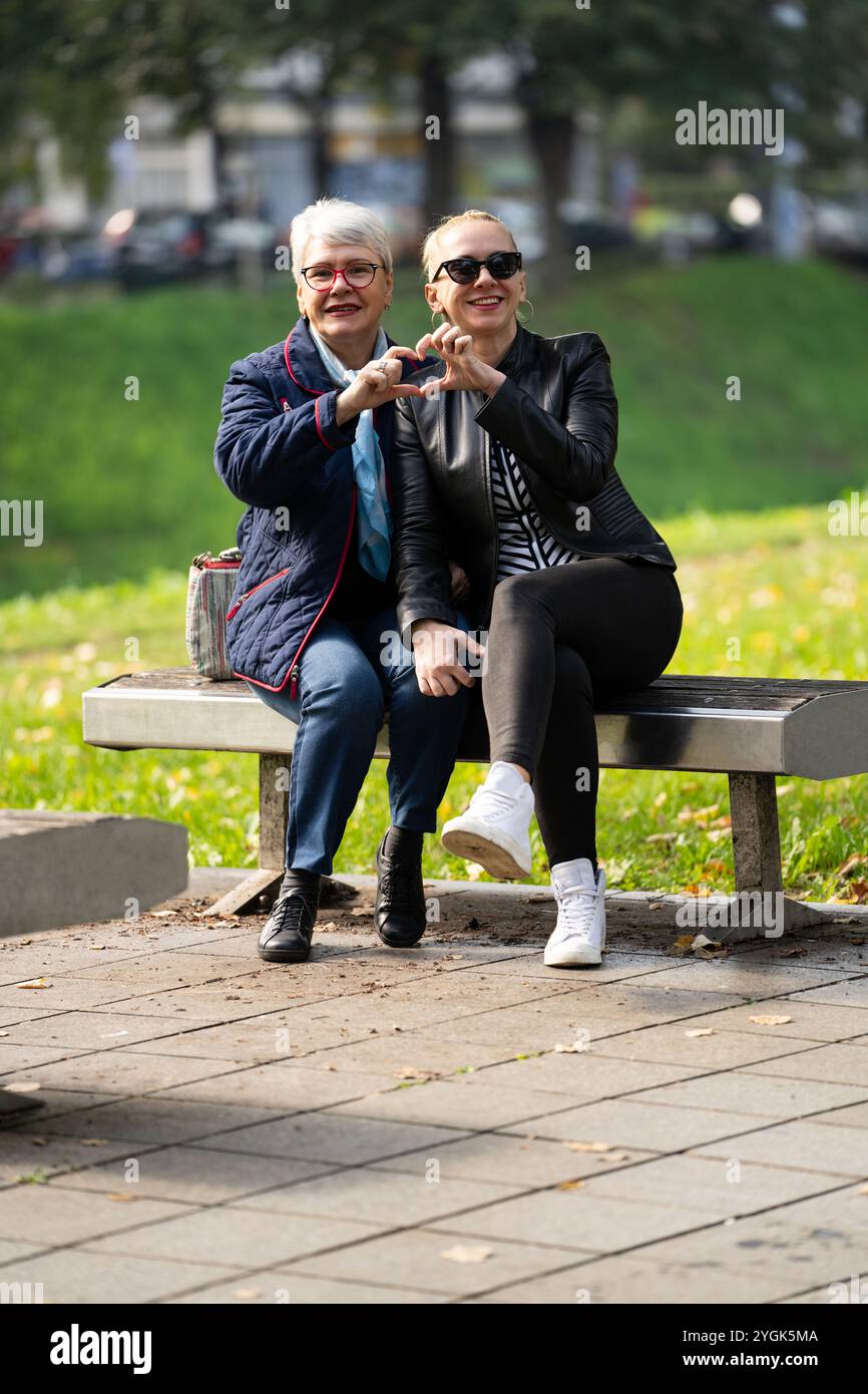 A senior mother and her daughter, casually dressed, sit together on a ...