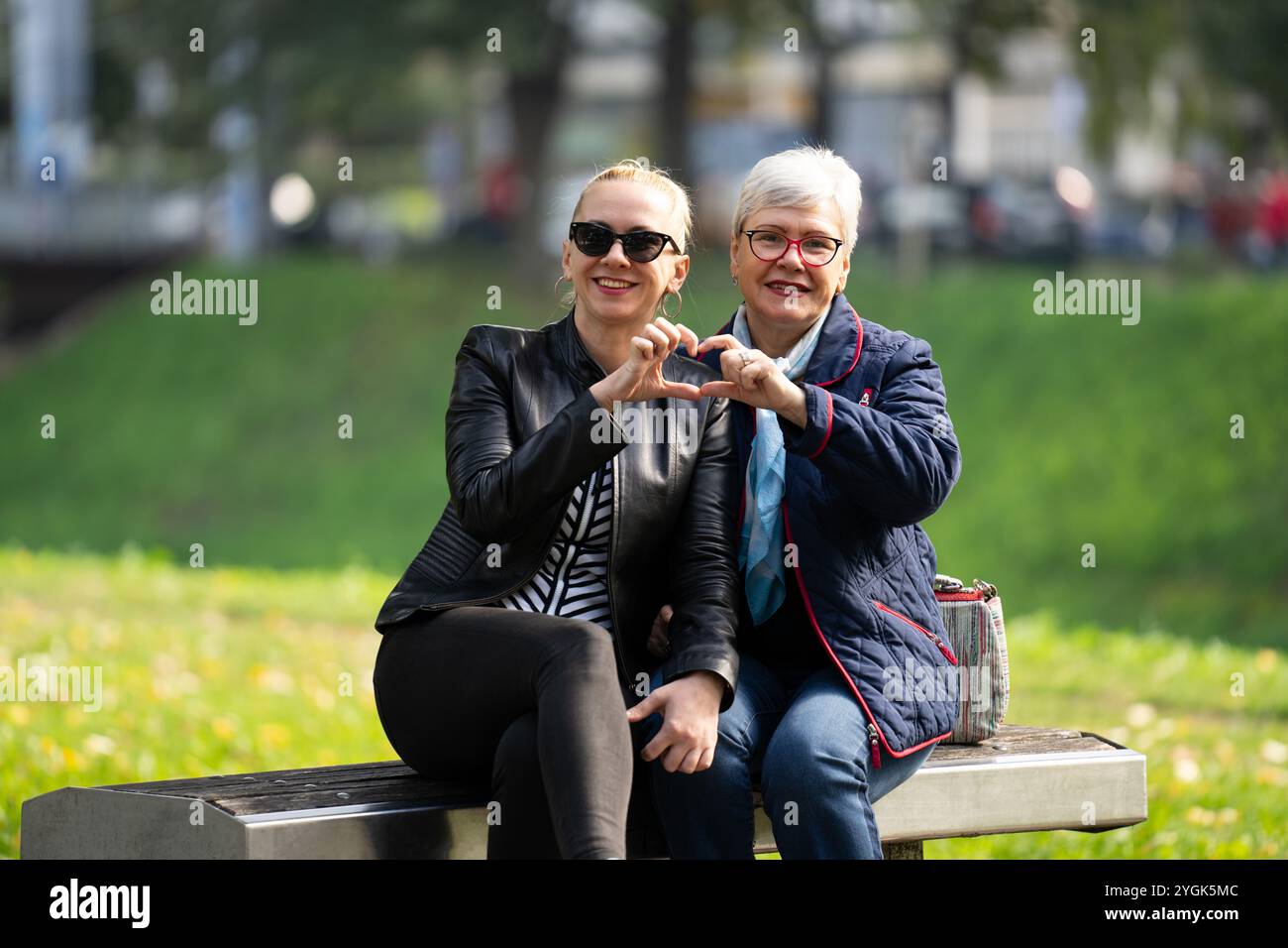 A gray-haired senior and her daughter relax in a park, enjoying the ...