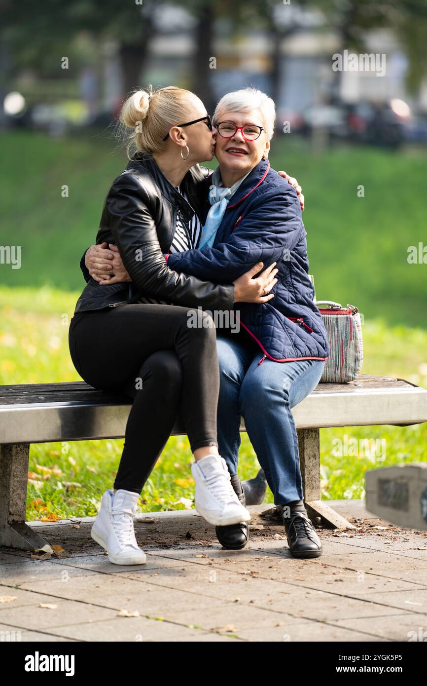 A senior mother and her daughter seated on a bench, sharing a joyful moment. The peaceful ...