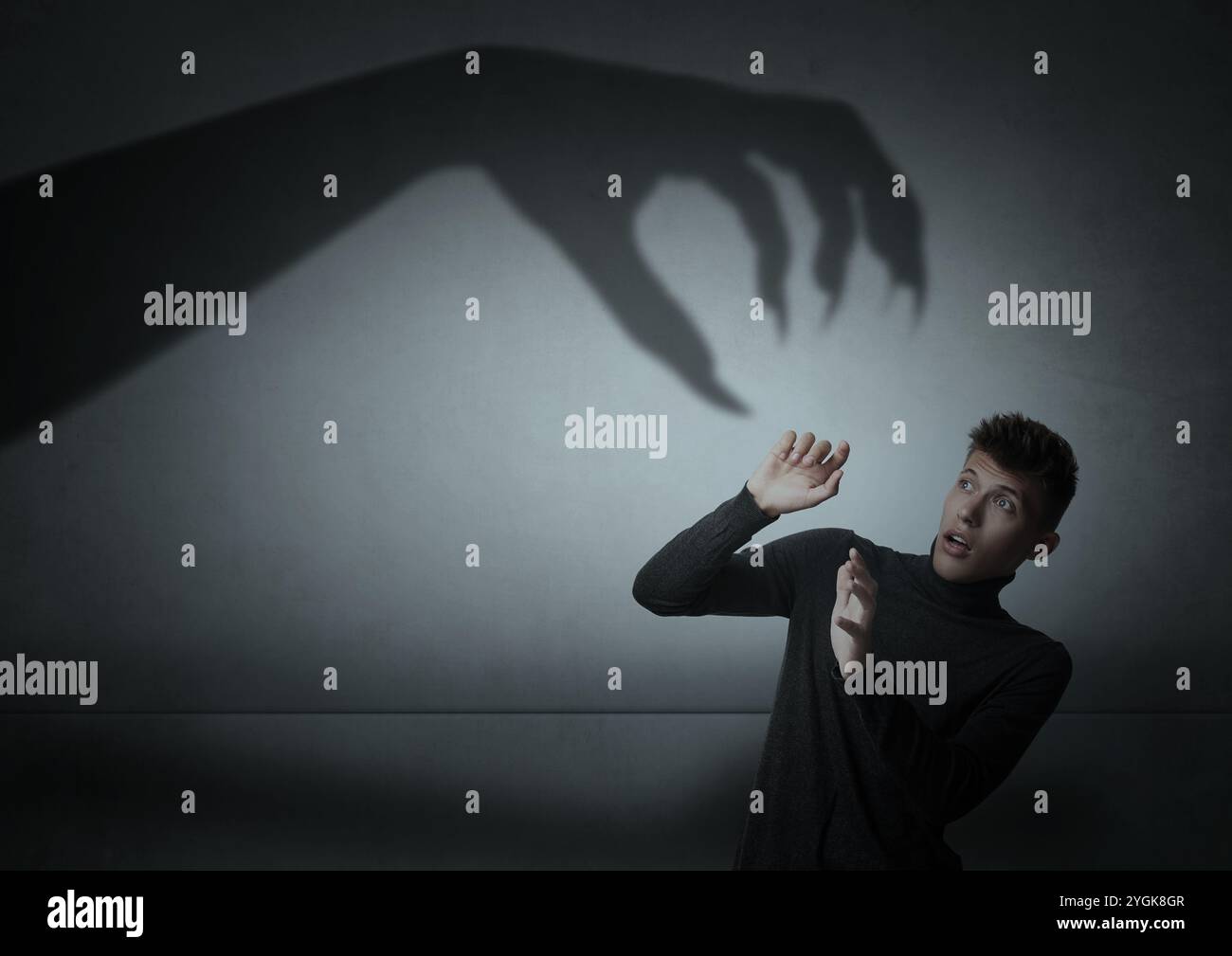 Young man scared by monstrous hand reaching for him. Creepy shadow on ...