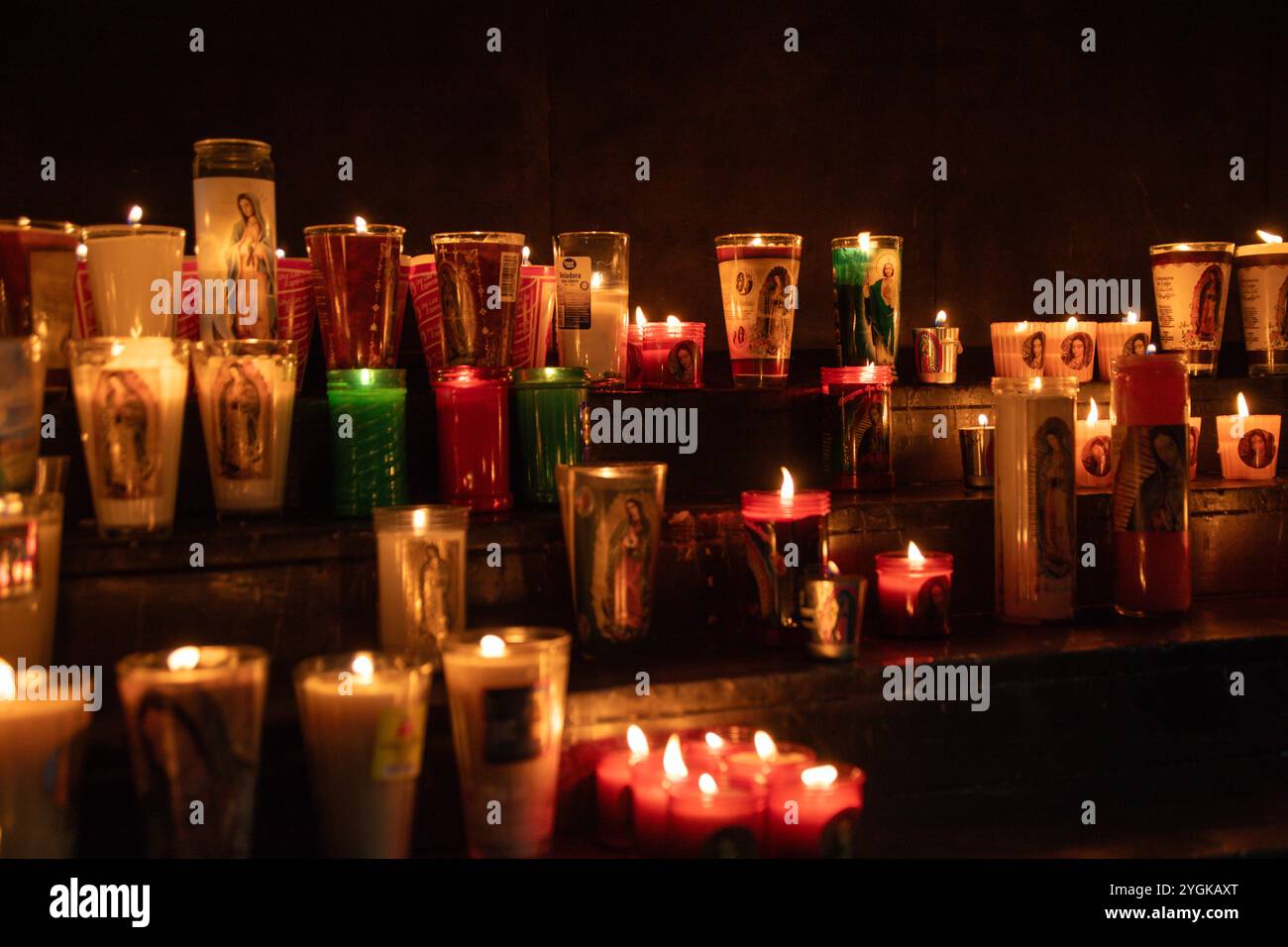Candles with religious images, casting a warm glow in a dark setting at ...
