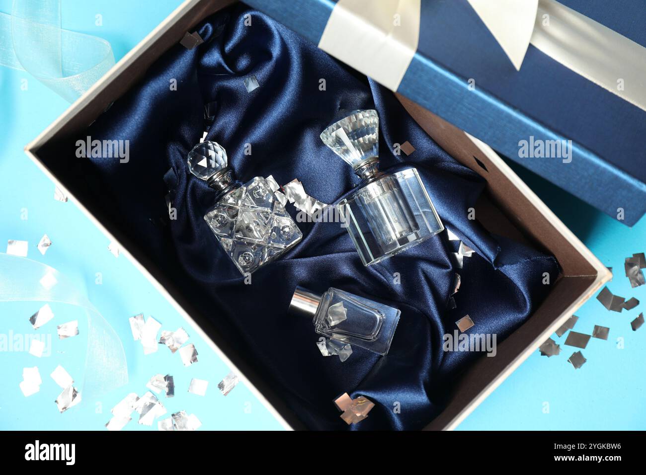 Perfume bottles in gift box and confetti on light blue background, top ...