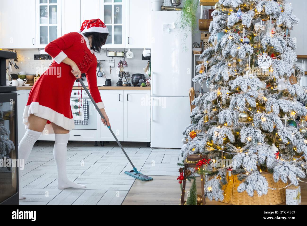 A woman in a red dress and Santa hat cleans the floor with a mop in a ...