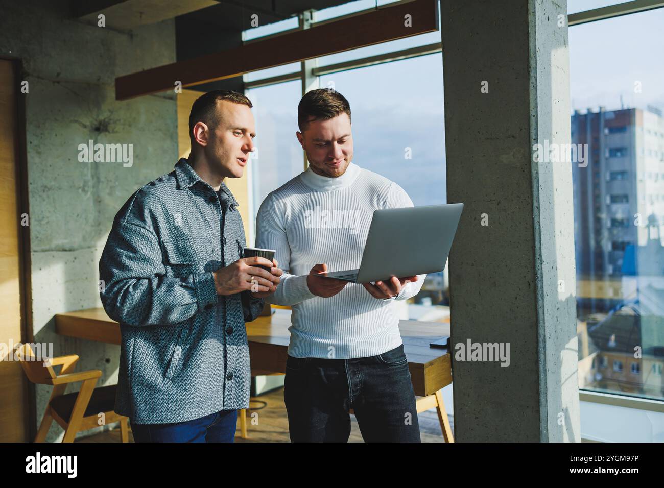 Work of two male colleagues standing in office together while ...
