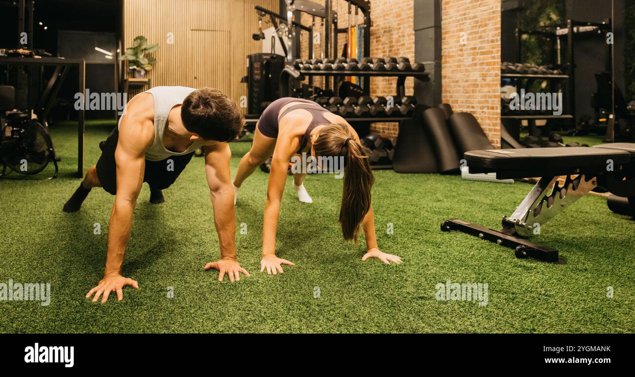 Two people exercising in a modern gym, performing bodyweight exercises ...