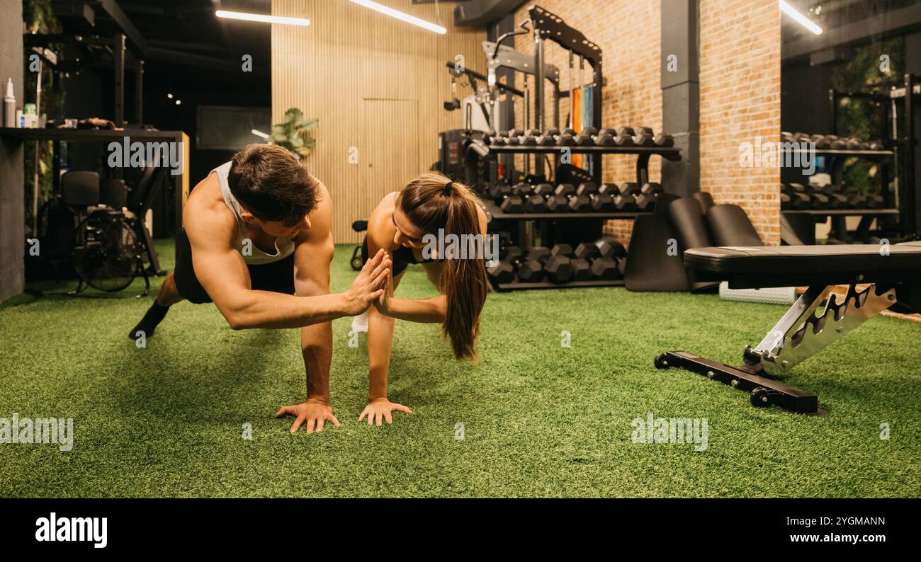 Two people high-fiving while doing planks in a modern gym. The ...