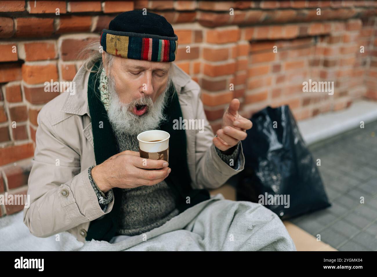 Closeup of frozen retired homeless man sitting on city street, holding ...