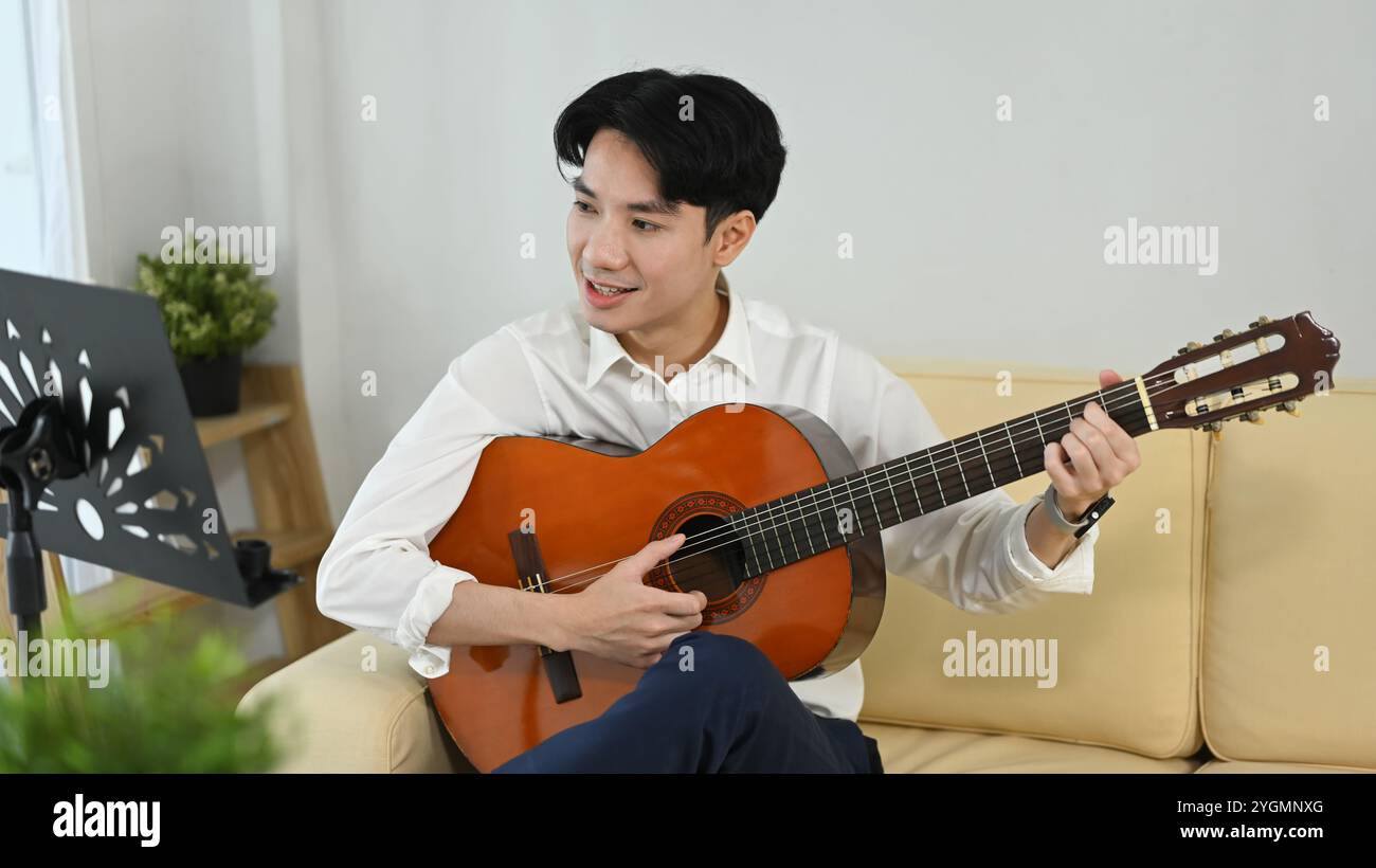 Smiling young man playing acoustic guitar with sheet music stand in the ...