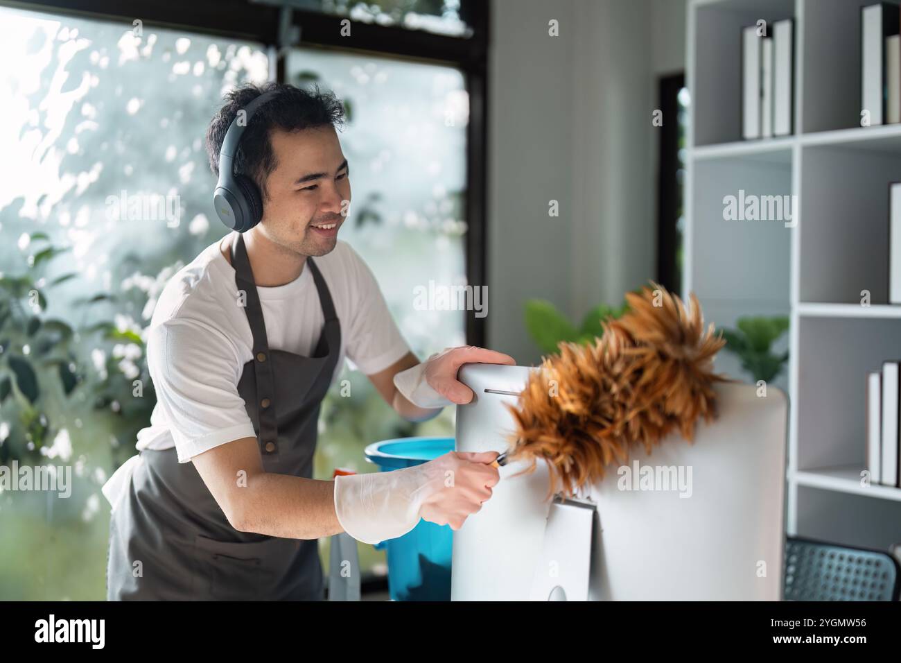 Smiling Man Cleaning Office Desk with Feather Duster and Headphones in ...
