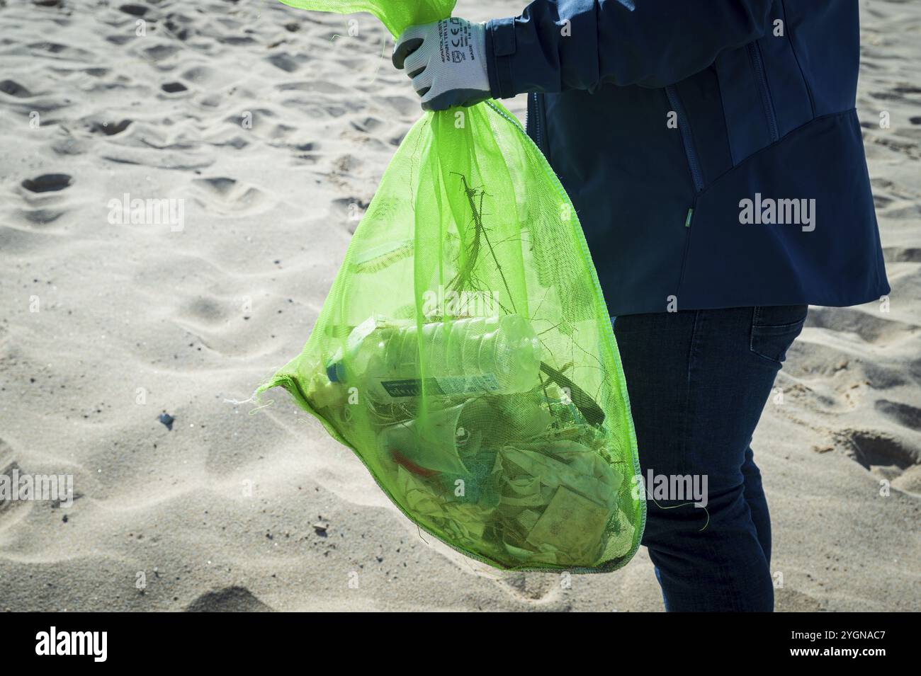 Person collecting rubbish on the beach in a green net, plastic waste ...