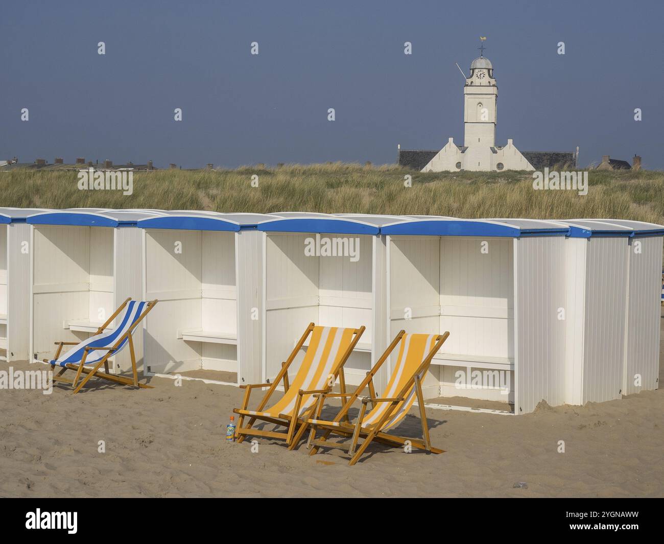 Deckchairs in front of beach cabins, with a lighthouse in the distance ...