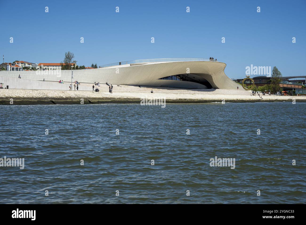 Modern, curved building by the river with blue sky and visitors, MAAT ...