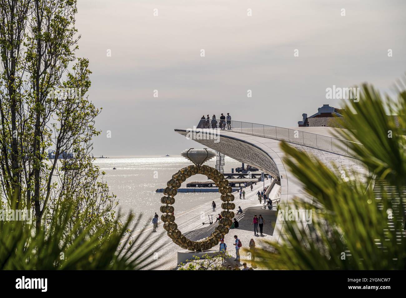 Walkers on a modern riverside path with sculptural element and plants ...