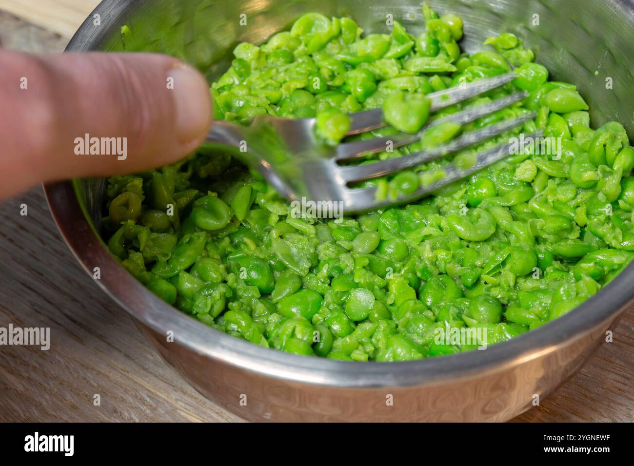 Person mushing garden peas using the back of a fork in a metal bowl ...