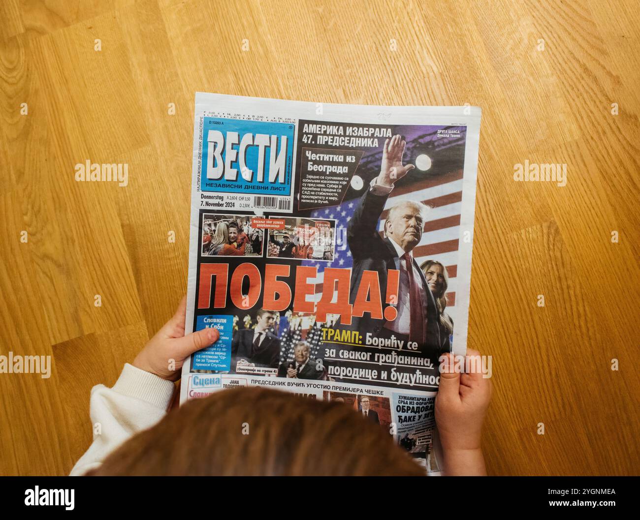 Paris, France - Nov 7, 2024: Curious toddler boy holding Serbian newspaper Vesti with the ...
