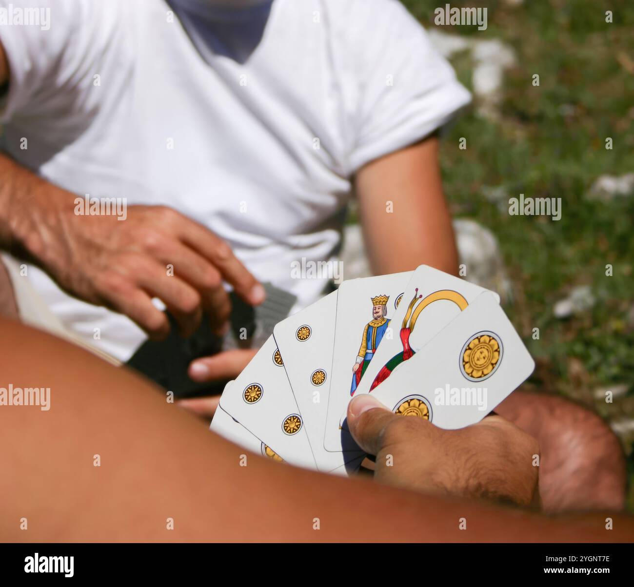 Two people playing cards outdoors during a summer day, holding a hand ...