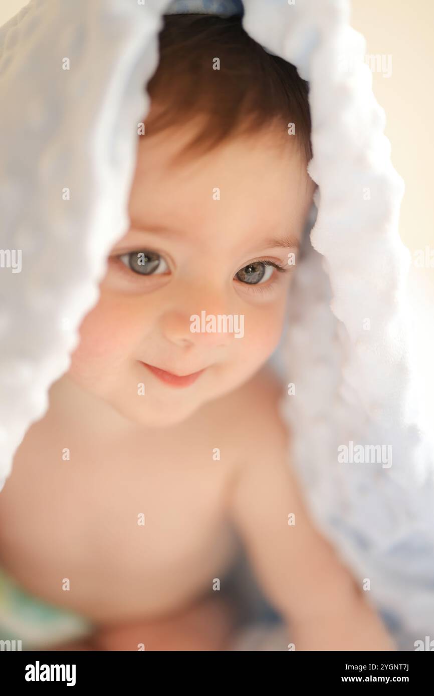 Adorable baby is hiding and smiling under a soft white towel after bath ...