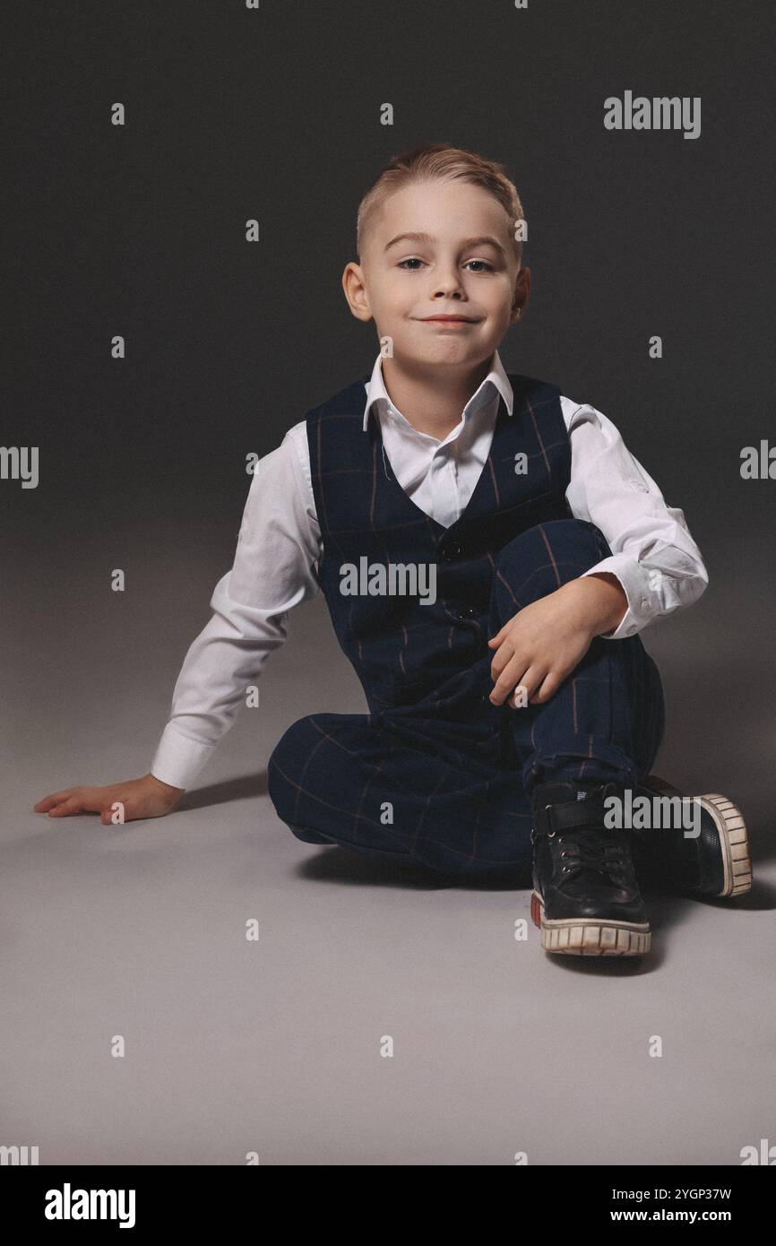 A handsome boy in a stylish outfit smiles, looks at the camera, poses ...
