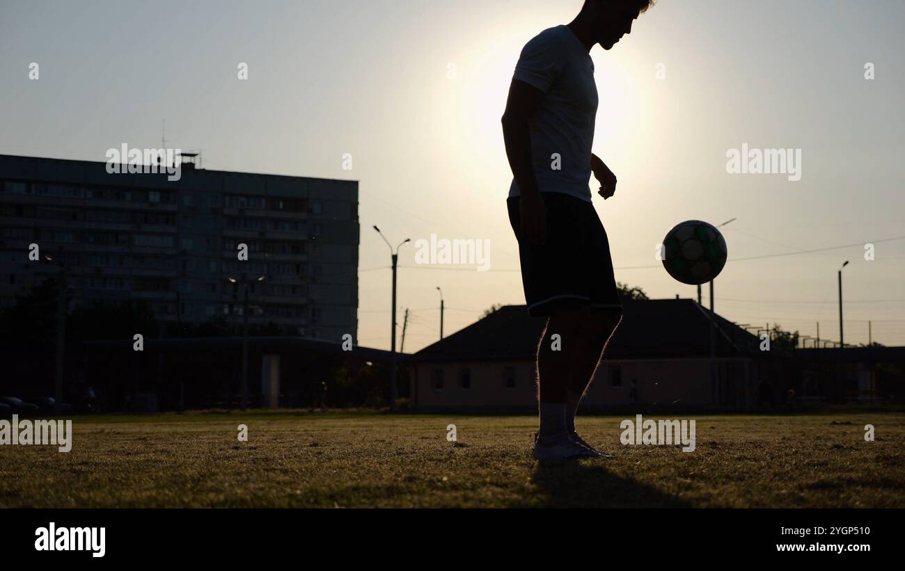 Professional footballer juggling soccer ball on stadium at sunset ...