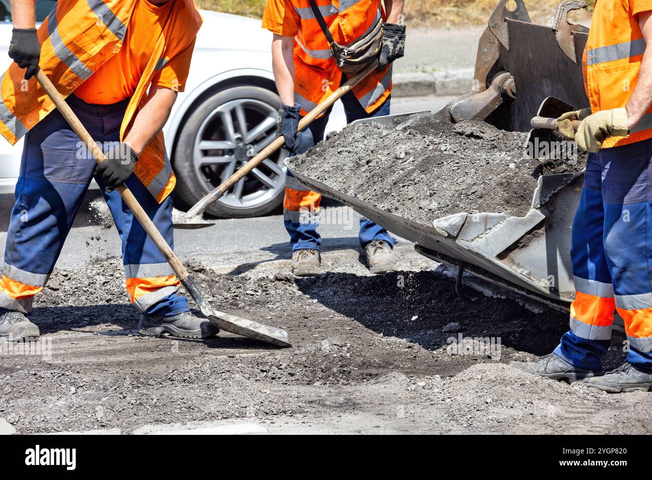 Workers repairing a road with asphalt under the midday sun in an urban ...