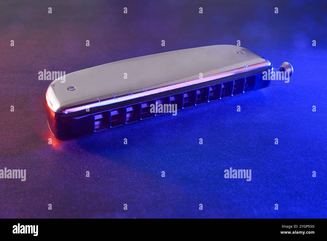 Metal and plastic chromatic harmonica of concert on a textured black table illuminated with red ...