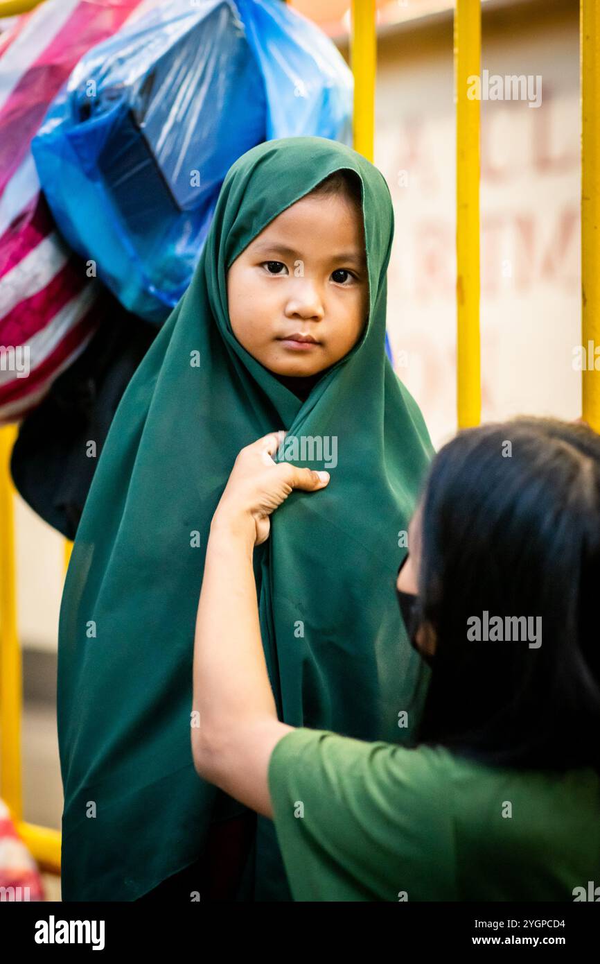 A young Muslim Filipino girl is dressed by her mother in the clothing ...