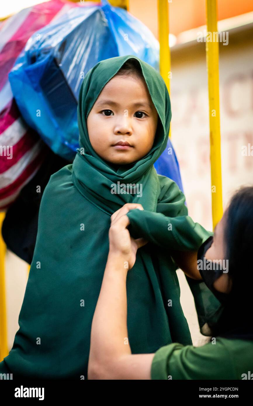 A young Muslim Filipino girl is dressed by her mother in the clothing ...