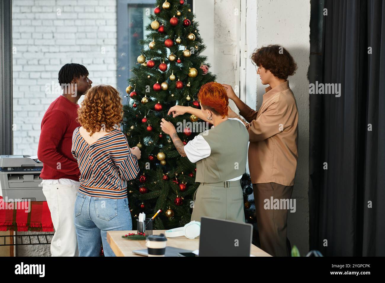 Coworkers embrace the festive spirit while decorating a Christmas tree ...