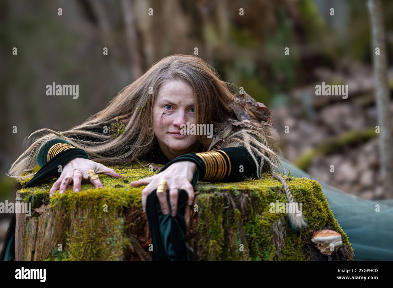 A woman leans on a moss-covered tree trunk in a forest. Shallow depth ...