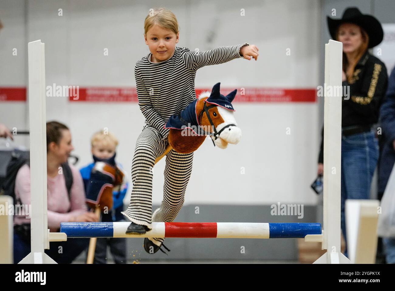 Six year old Lina jumps on a stick horse over an obstacle at a hobby ...