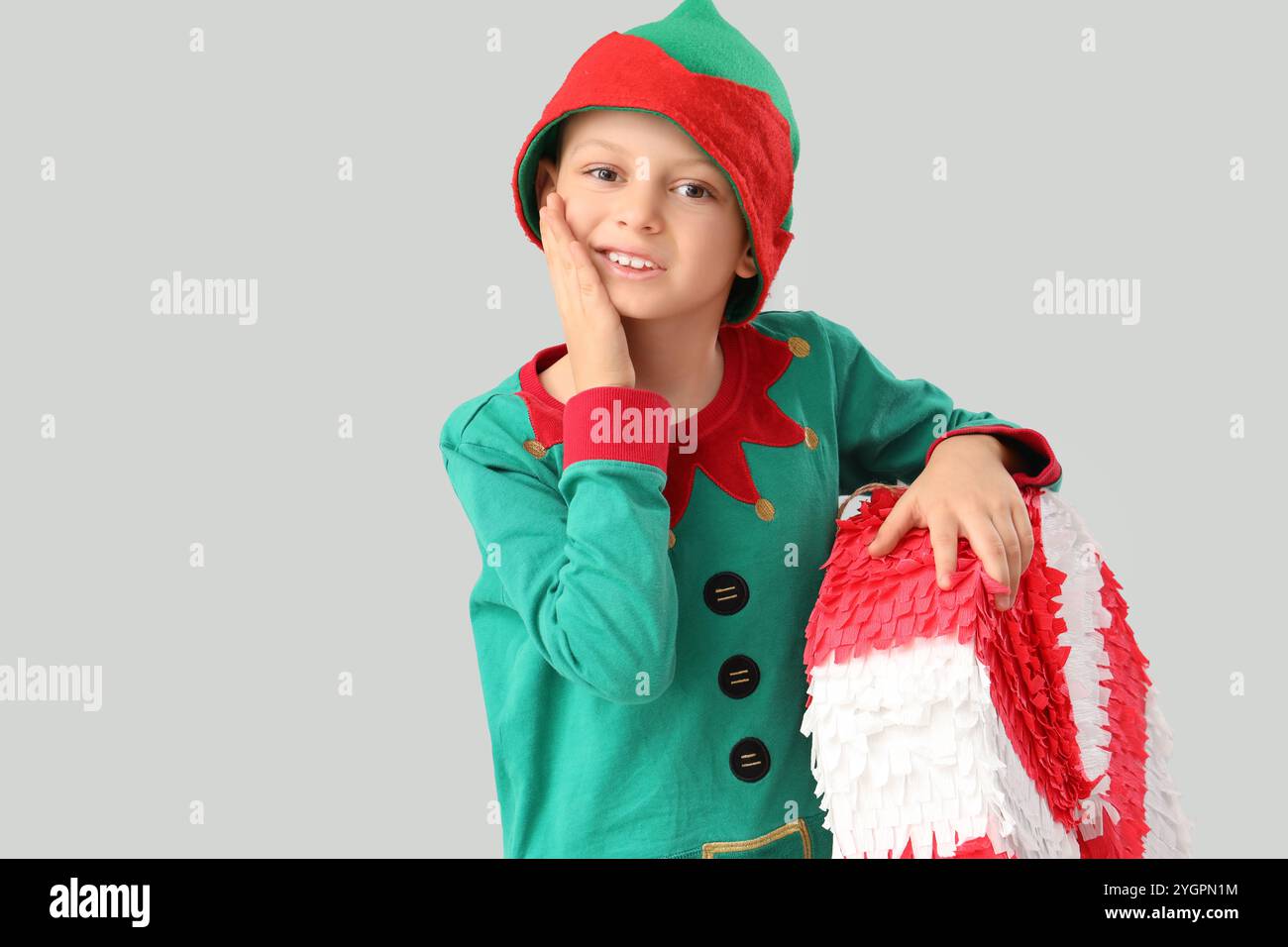 Cute little boy in elf's costume with candy cane pinata on grey ...