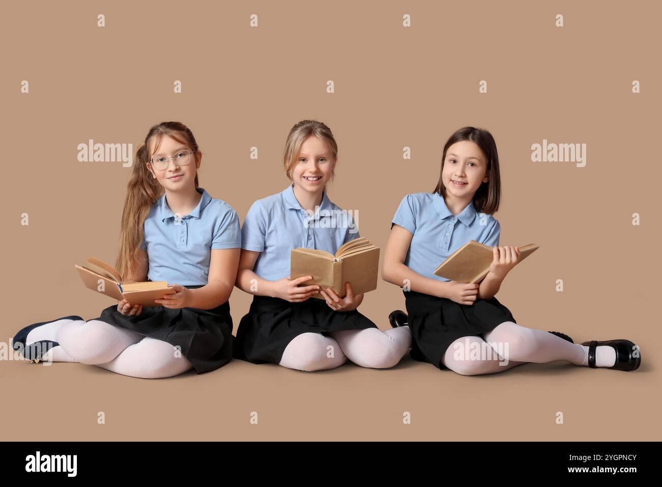 Cute girls in school uniform reading books on beige background Stock ...
