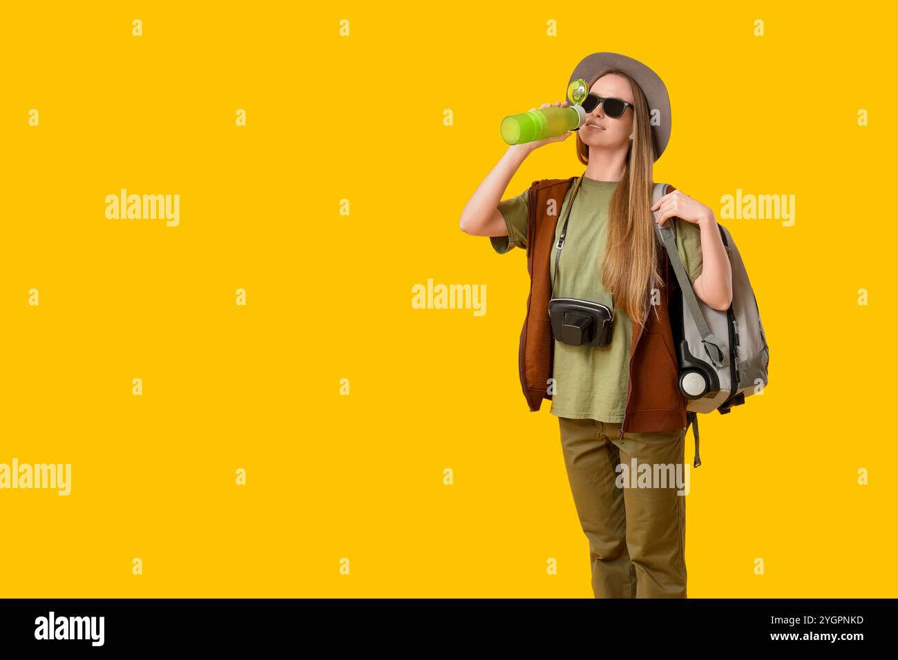 Young woman drinking something from plastic bottle on yellow background ...