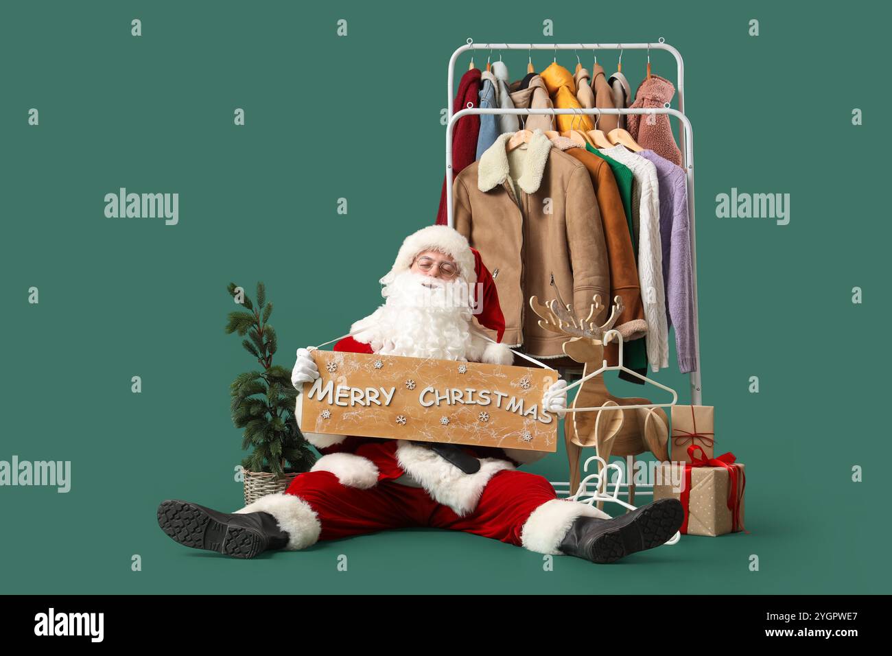 Santa Claus holding board with text MERRY CHRISTMAS near rack with ...