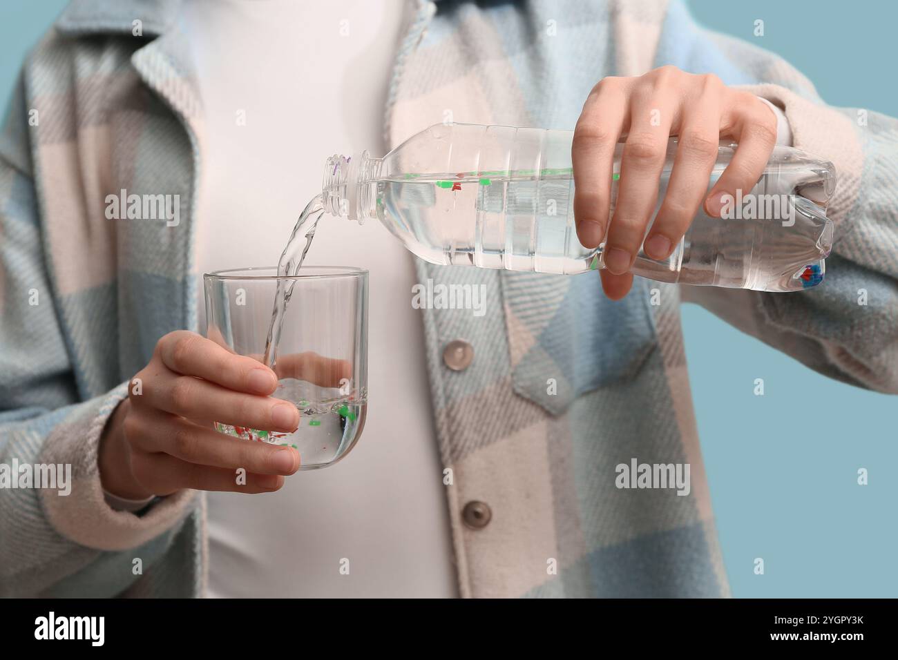 Woman pouring water with plastic into glass on blue background, closeup ...