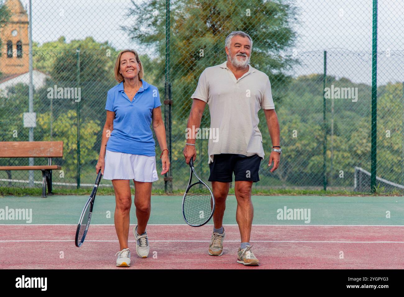 senior tennis couple walks together toward the camera, preparing for ...