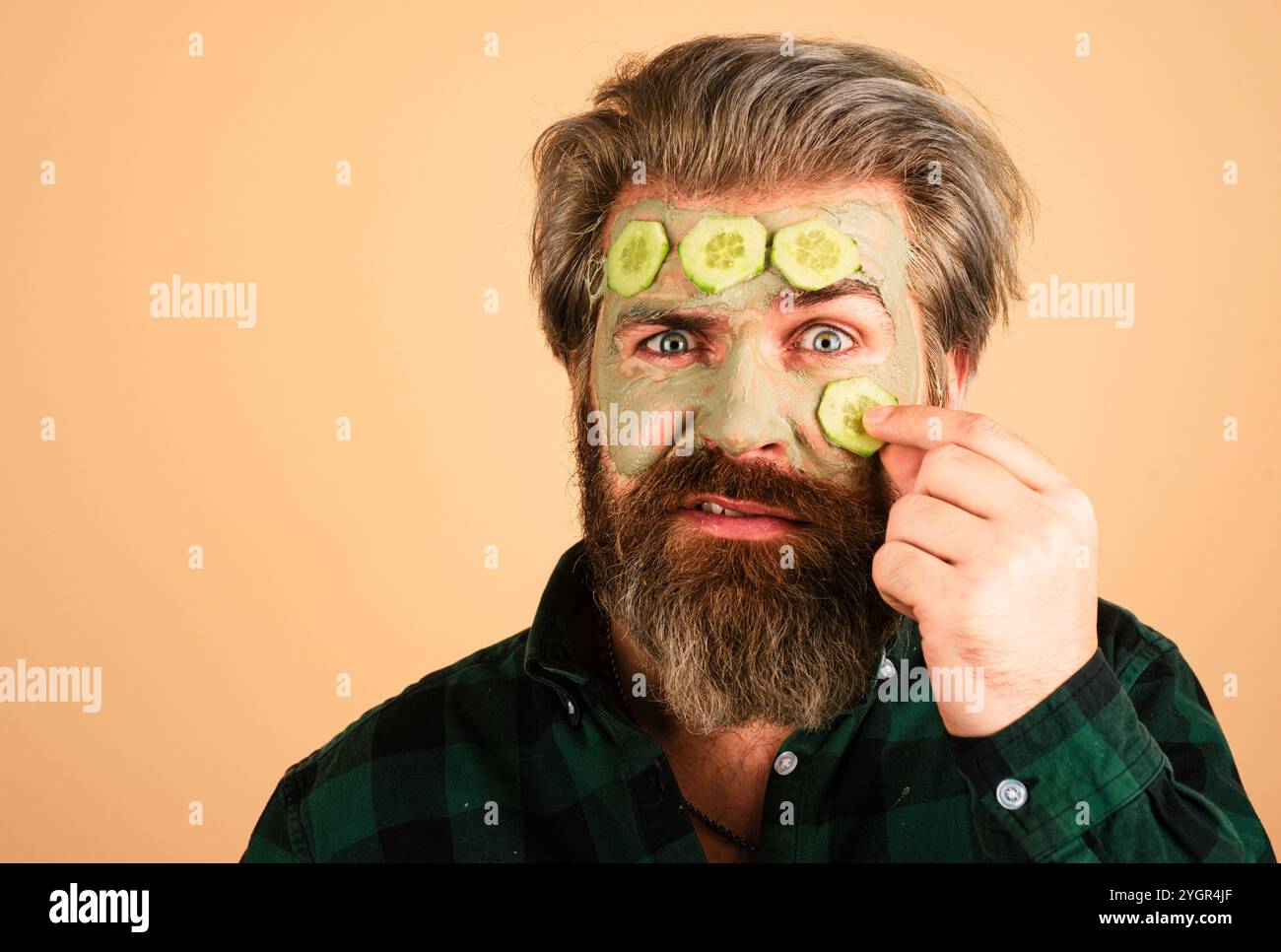 Funny male model with clay mask and cucumber slices on face. Spa ...