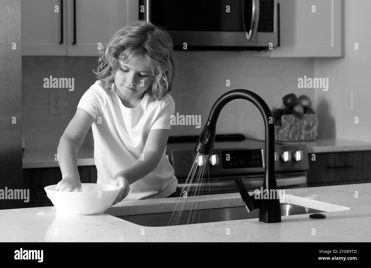 Child with sponge with dish washing liquid is doing the dishes at home ...