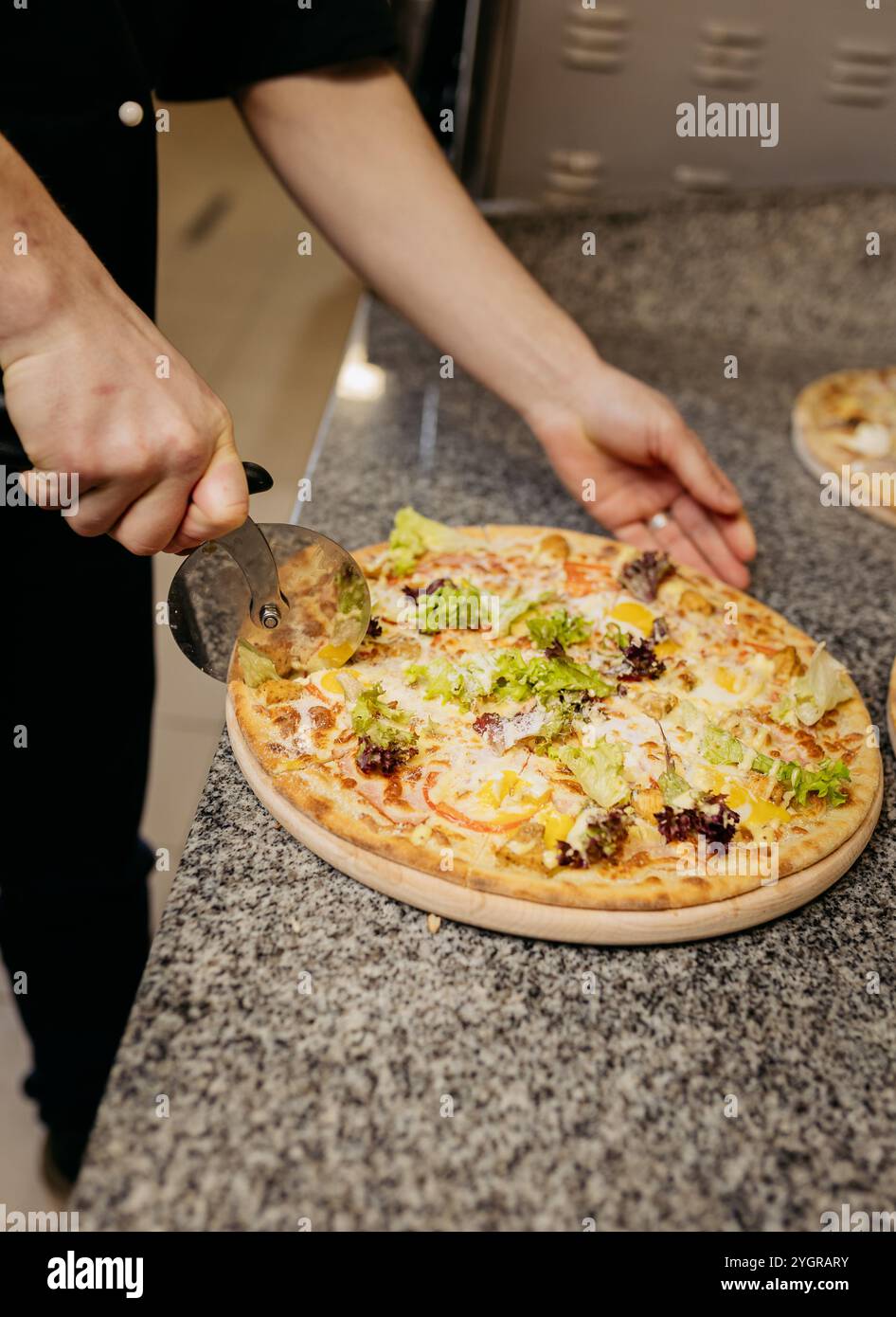 Chef slicing fresh vegetable pizza with pizza cutter on granite ...