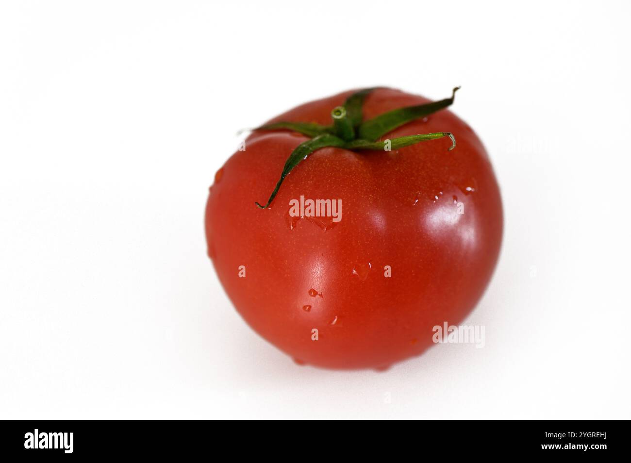 A vibrant, red tomato rests on a smooth surface, adorned with tiny ...